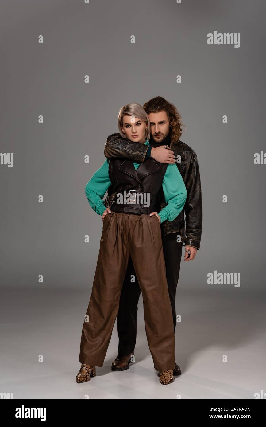 man in leather jacket hugging woman in vest on grey background Stock ...