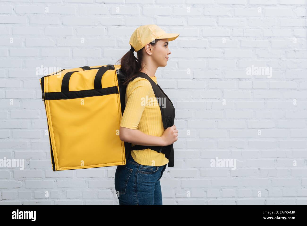 Side view of courier in yellow uniform with thermo backpack standing ...