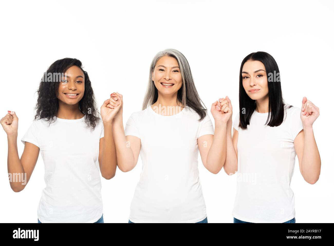 happy multicultural women looking at camera and holding hands isolated ...
