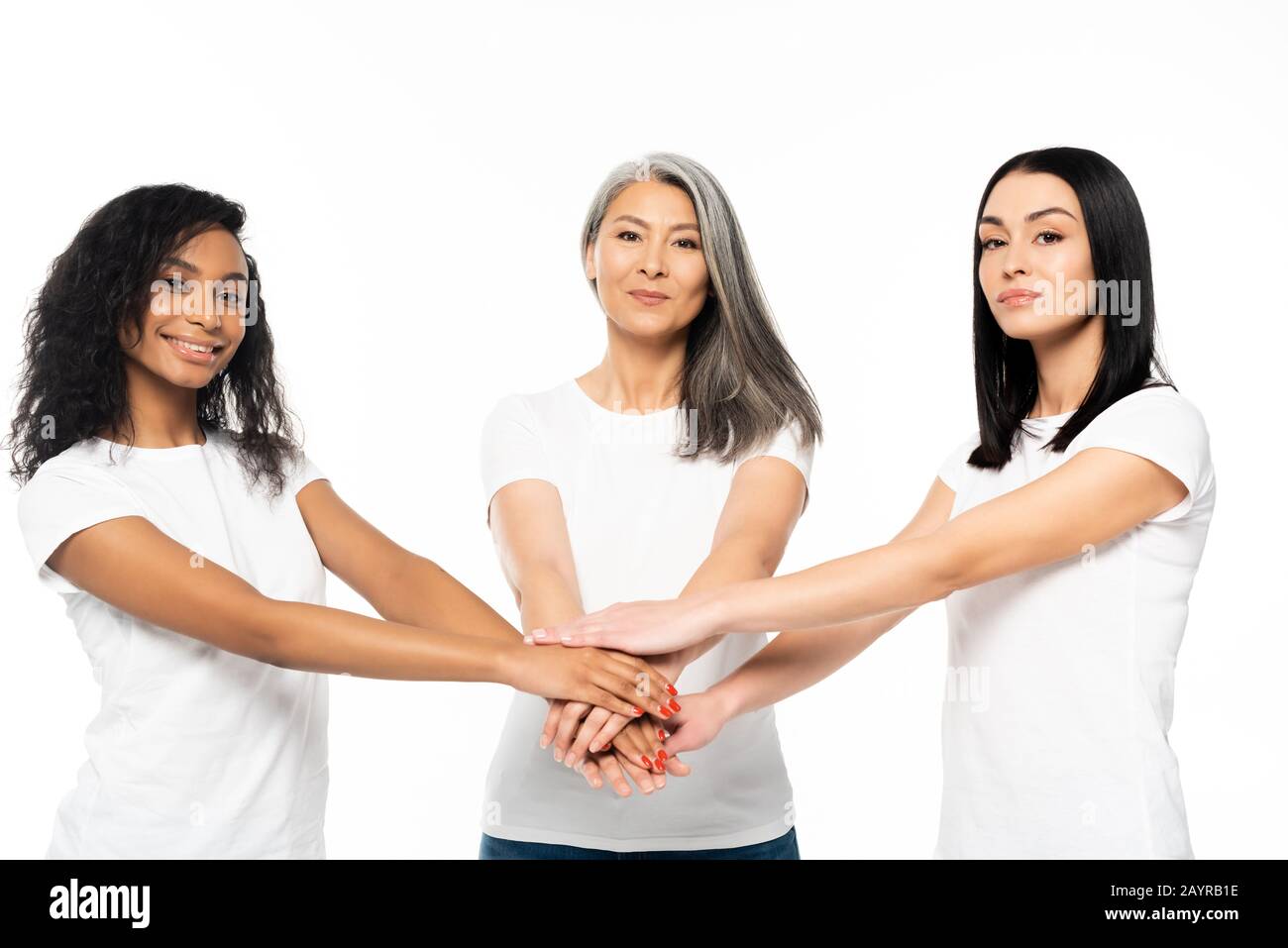 cheerful multicultural women putting hands together isolated on white ...