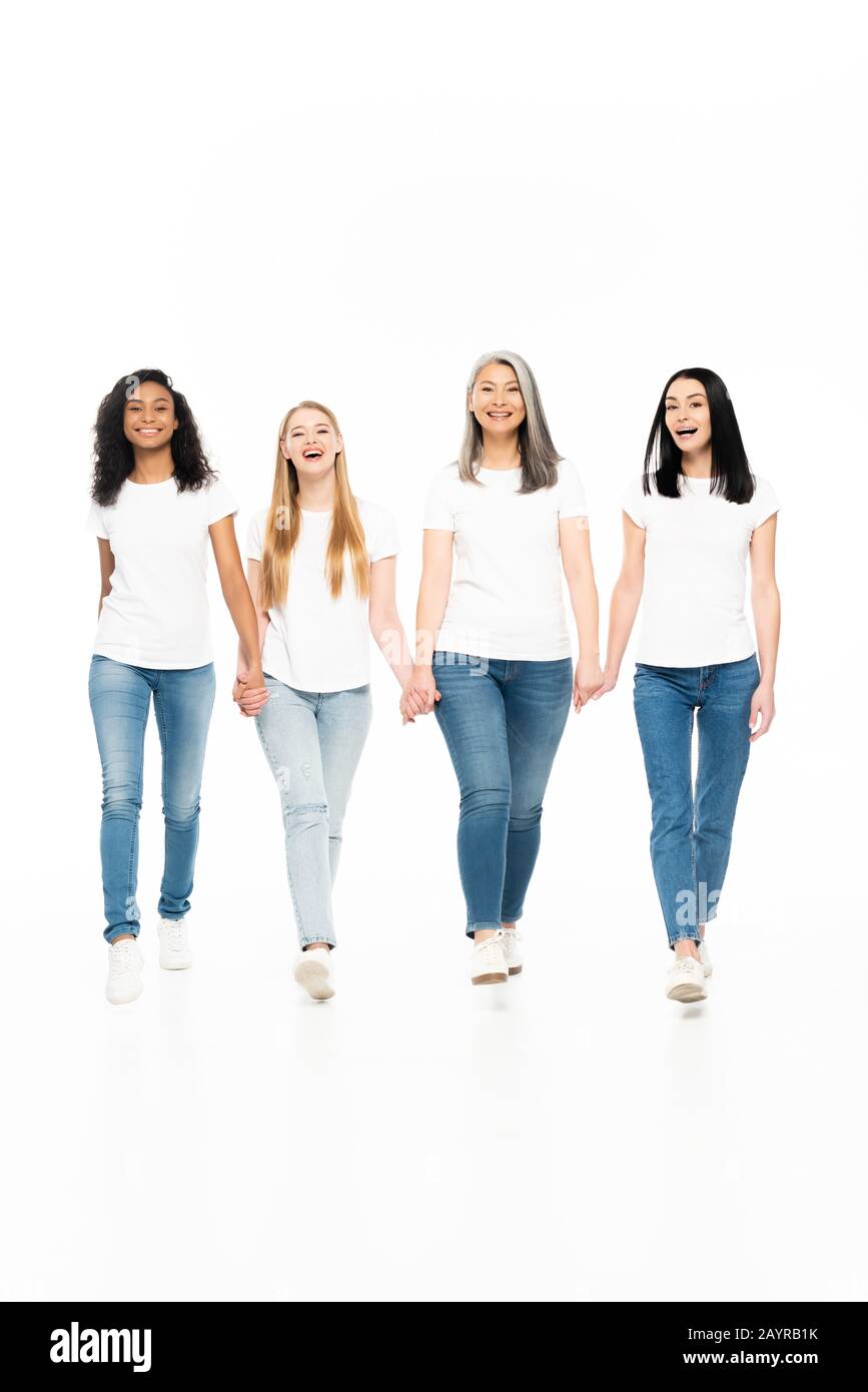 happy multicultural women in denim jeans walking and holding hands ...