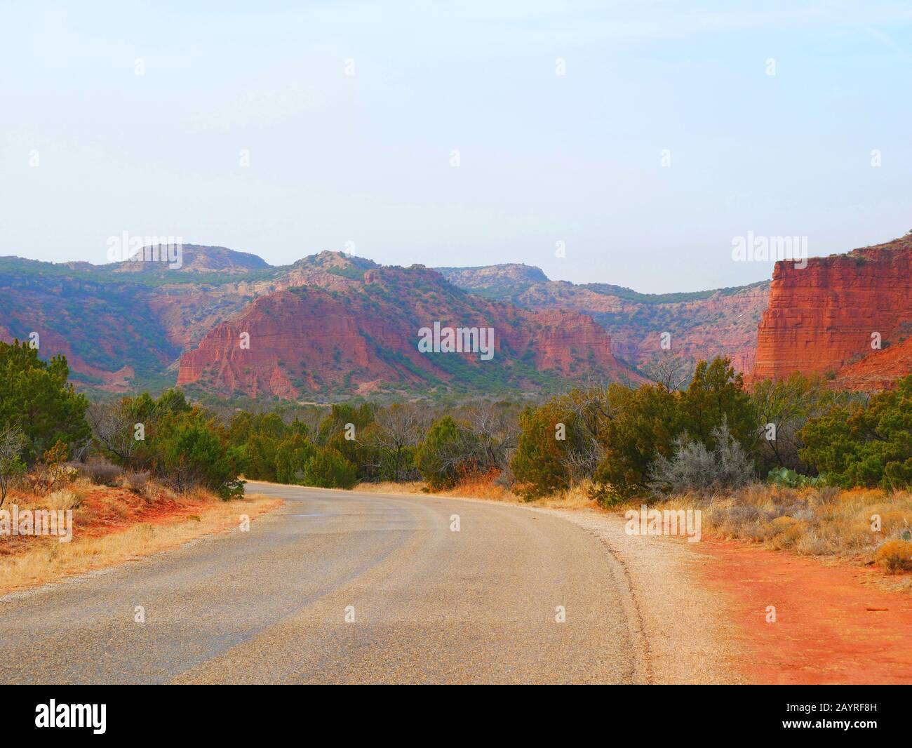 Beautiful red bluffs flank the winding country road surrounded by green ...