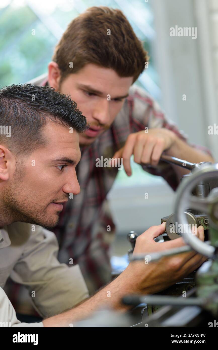 foreman checking metal component on machinery apprentice watching Stock ...