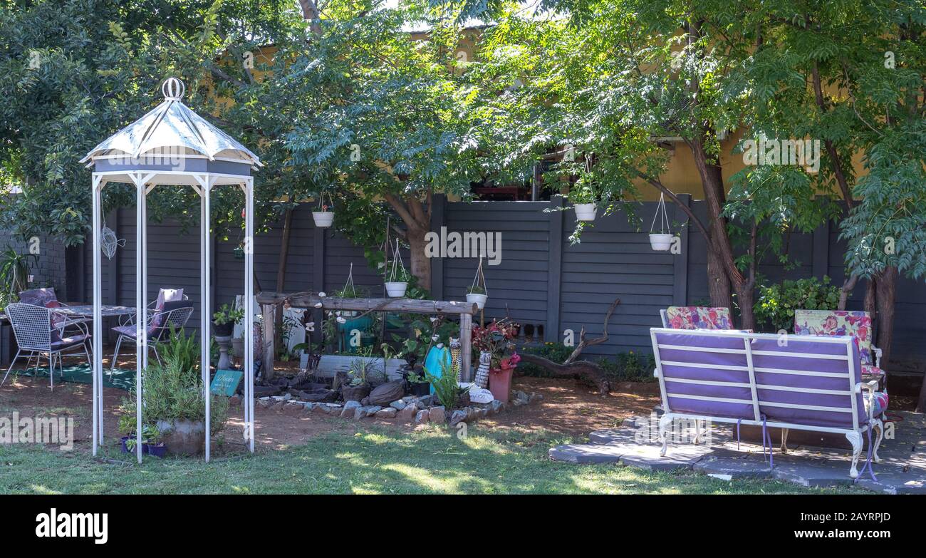 A quiet shady spot in a garden under trees with a bench and chairs ...