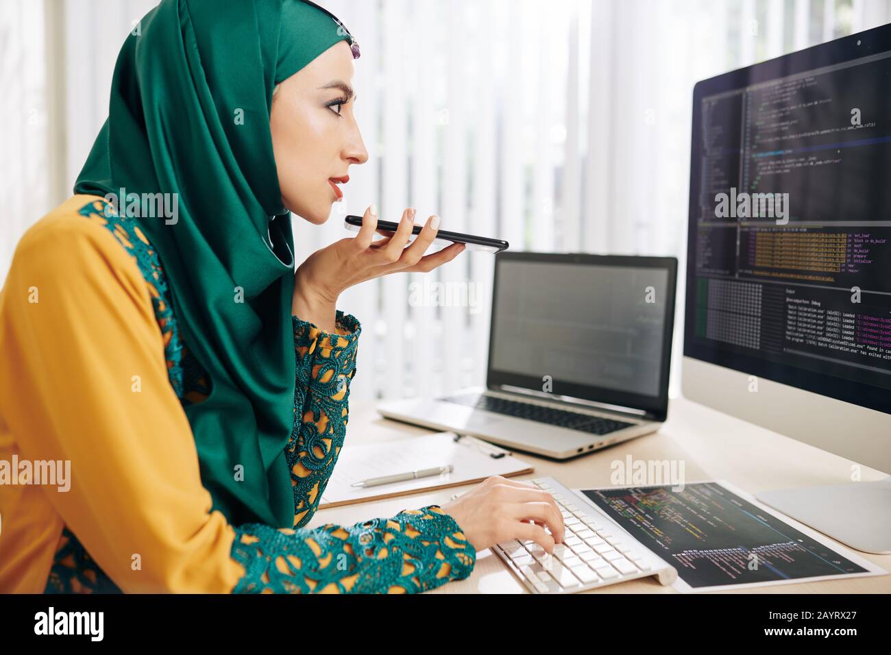 Beautiful young female programmer in hijab checking code on computer ...