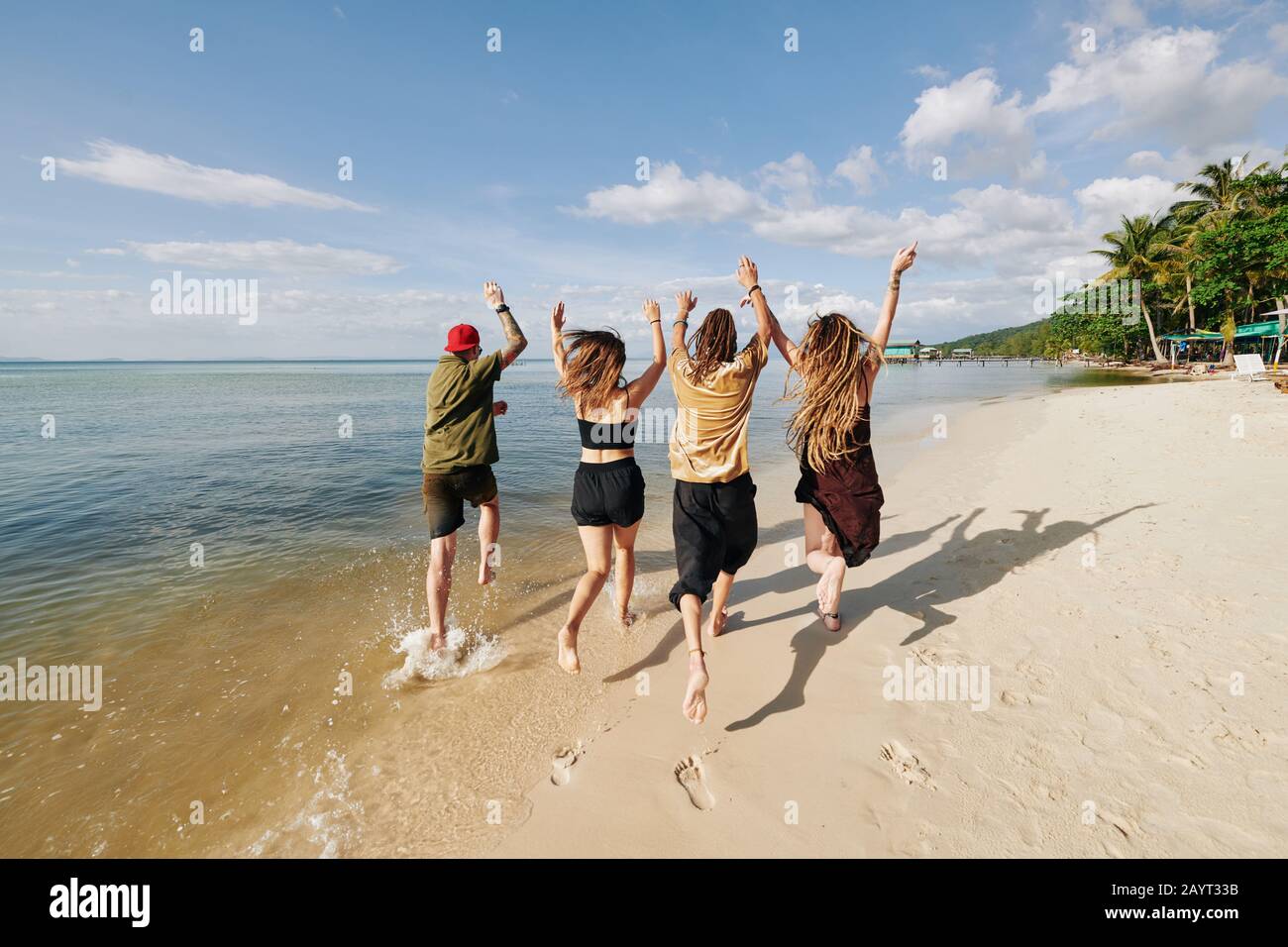 Group of happy excited young people raising arms and running on beach ...
