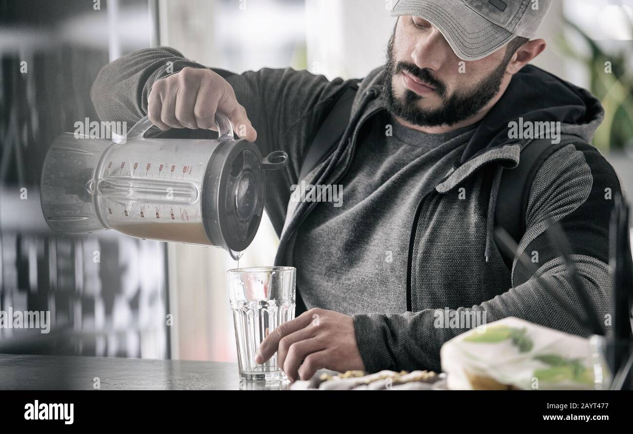 handsome young bearded male fill glass with fruit juice in fitness club ...