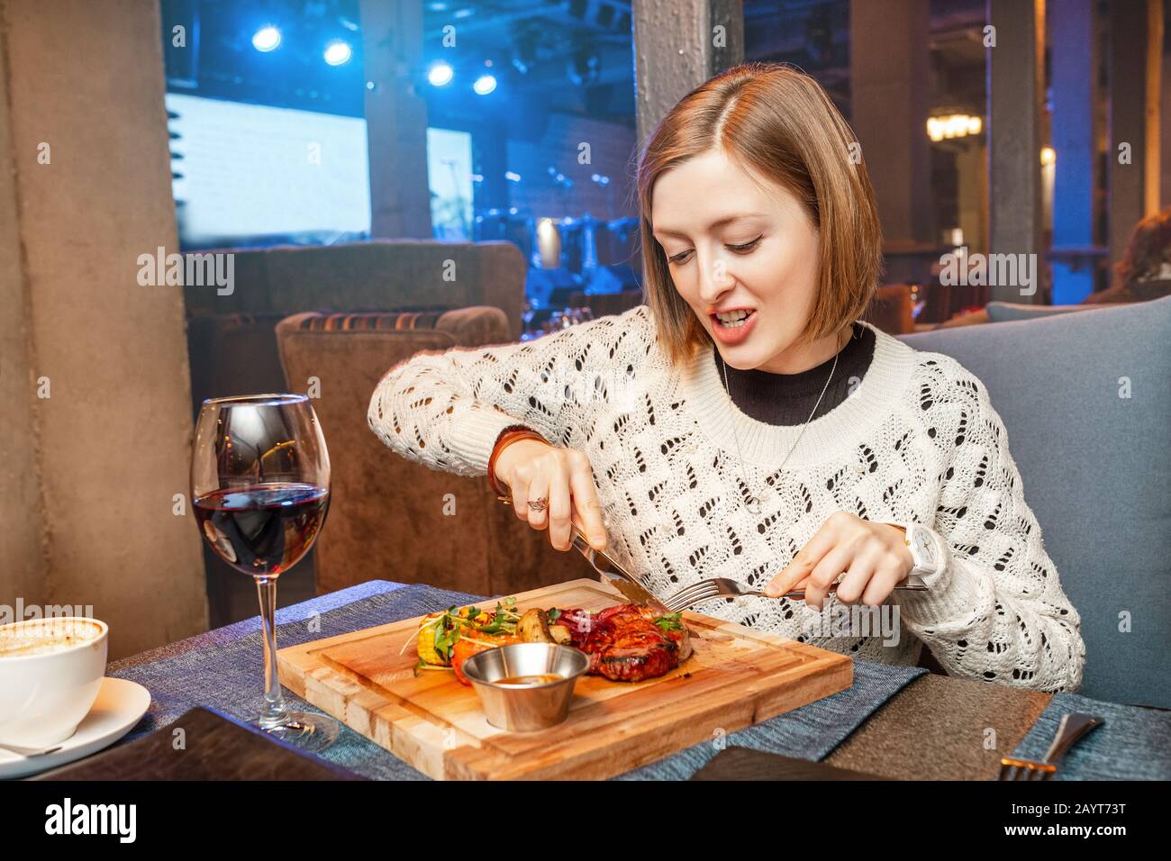 Woman eating meat steak and drinking wine in a restaurant in a ...