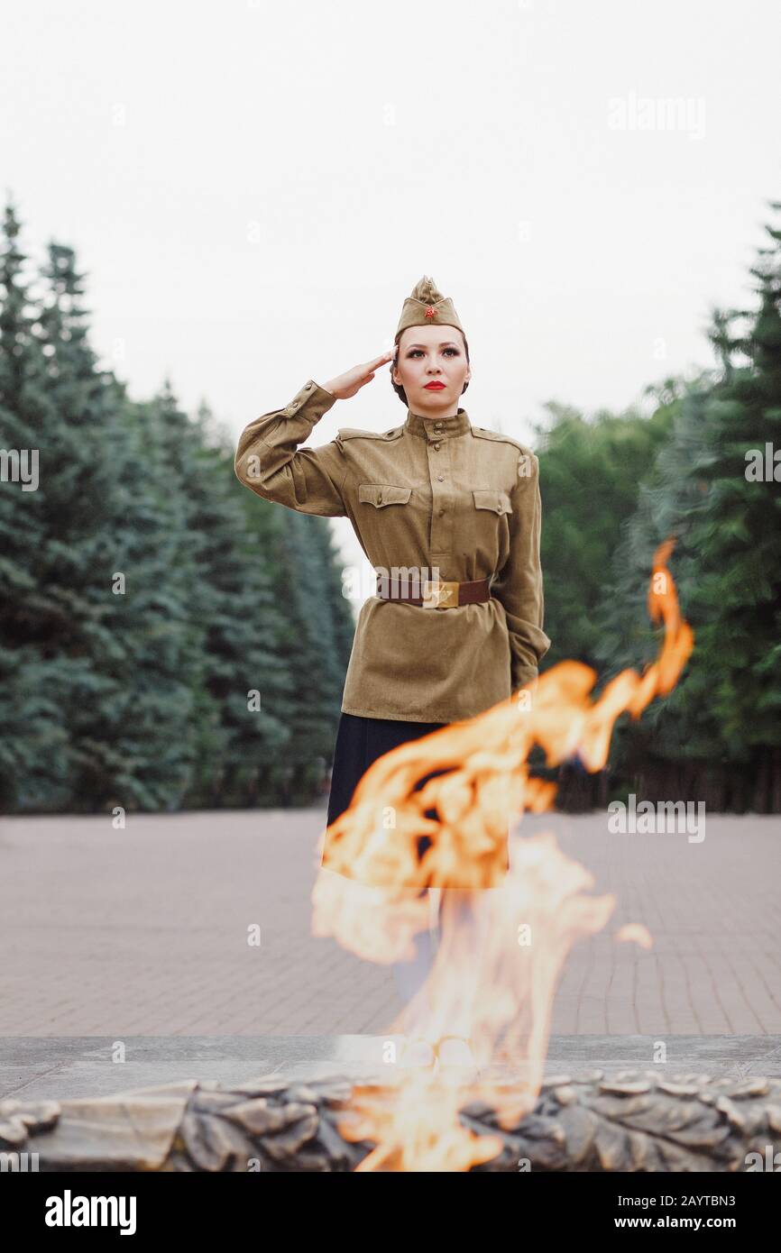 A girl in an old Soviet military uniform salute near the eternal flame ...