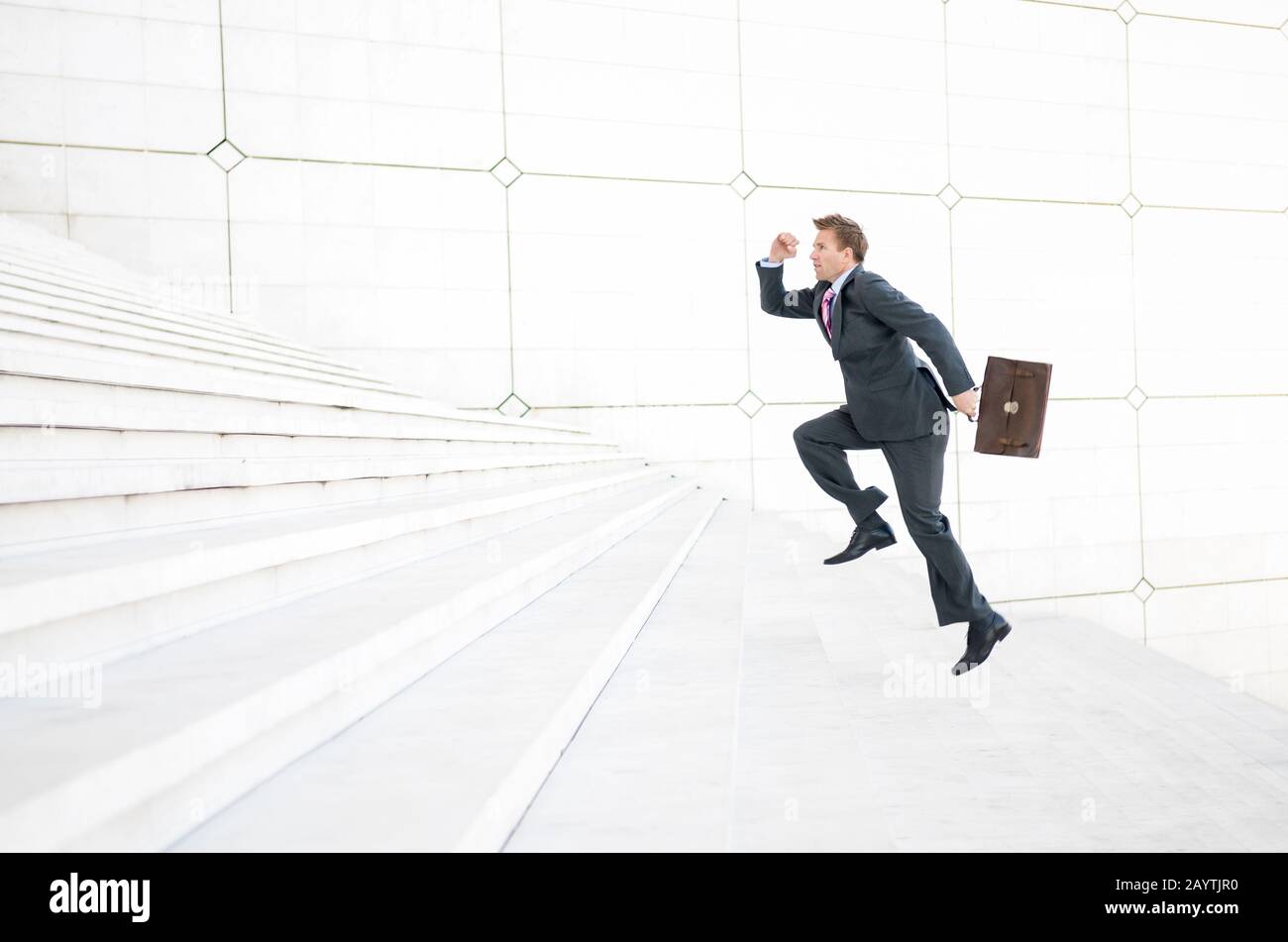 Businessman taking a dramatic run outdoors up a long white staircase ...