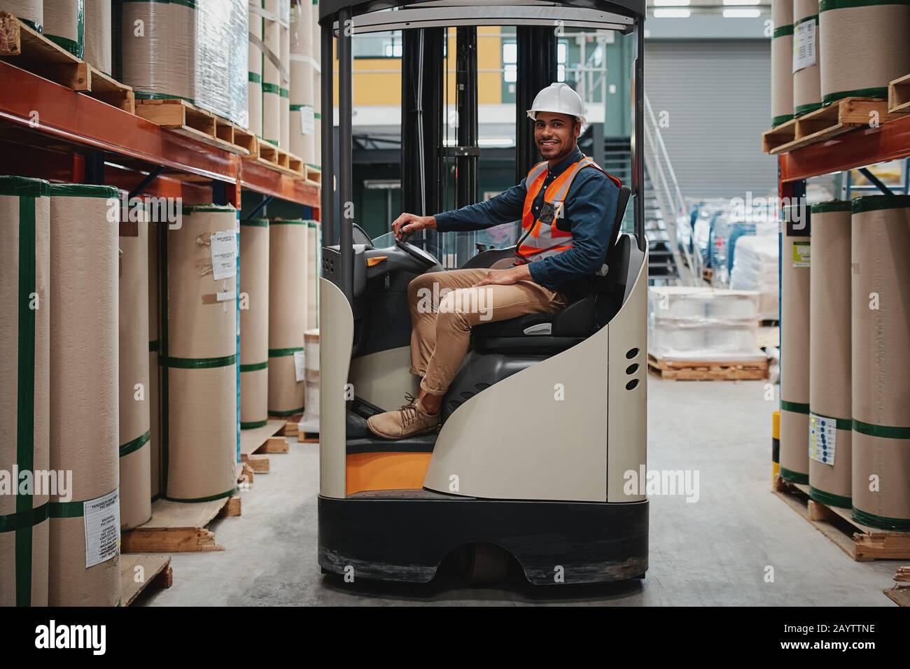 Smiling forklift driver wearing white helmet and vest sitting in ...