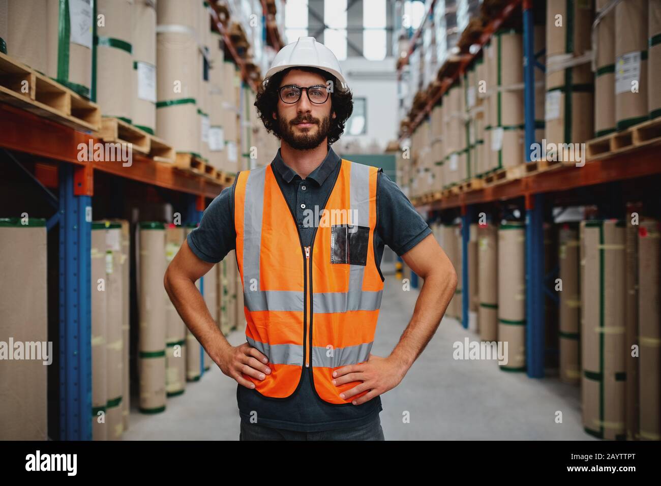 Confident warehouse manager standing in between shelf with hands on ...