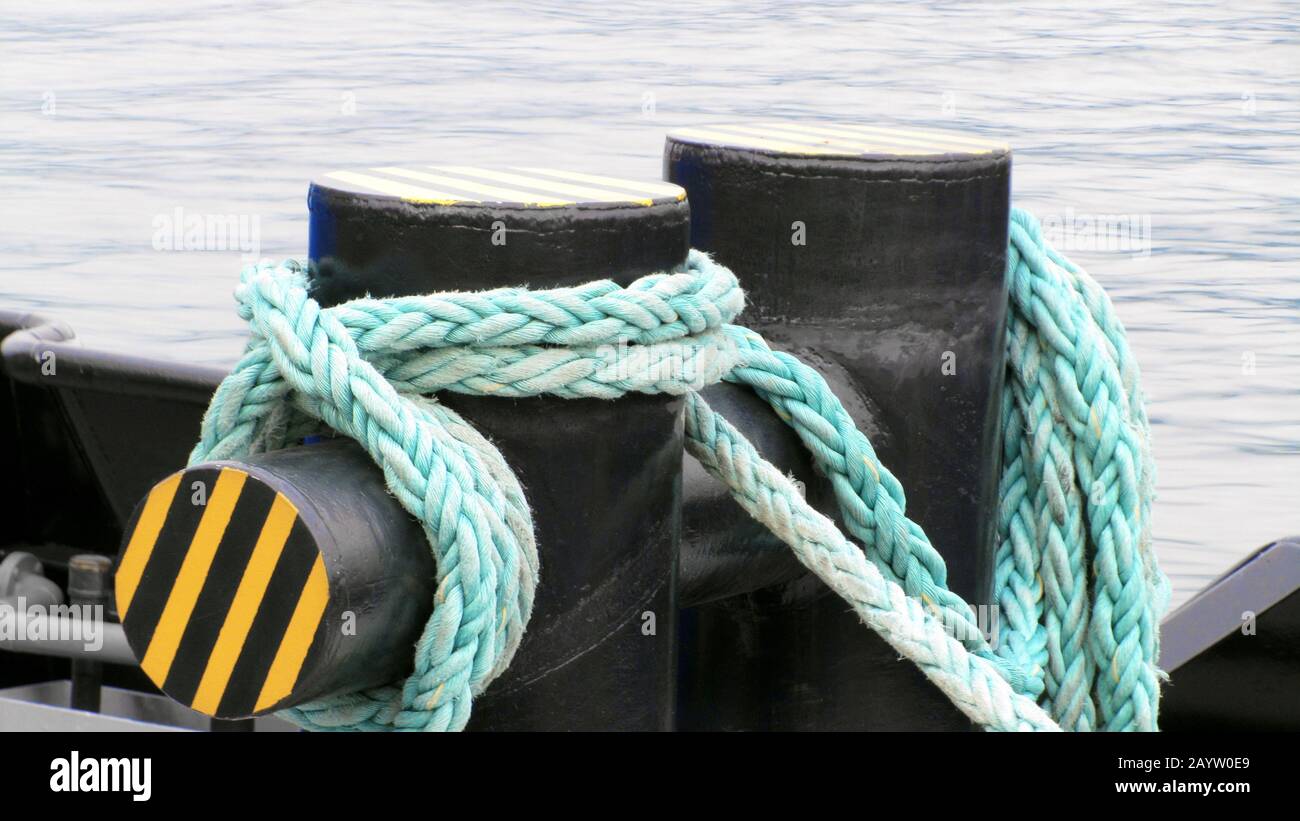 Bollard with mooring ropes. Black large metal pier stands alone amid ...
