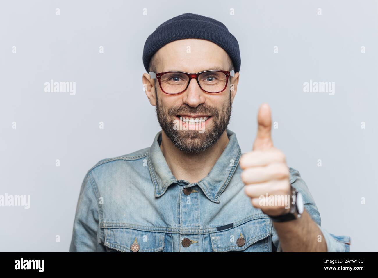 Positive middle aged male with thick beard and mustache, shows ok sign, raises thumb, dressed in ...