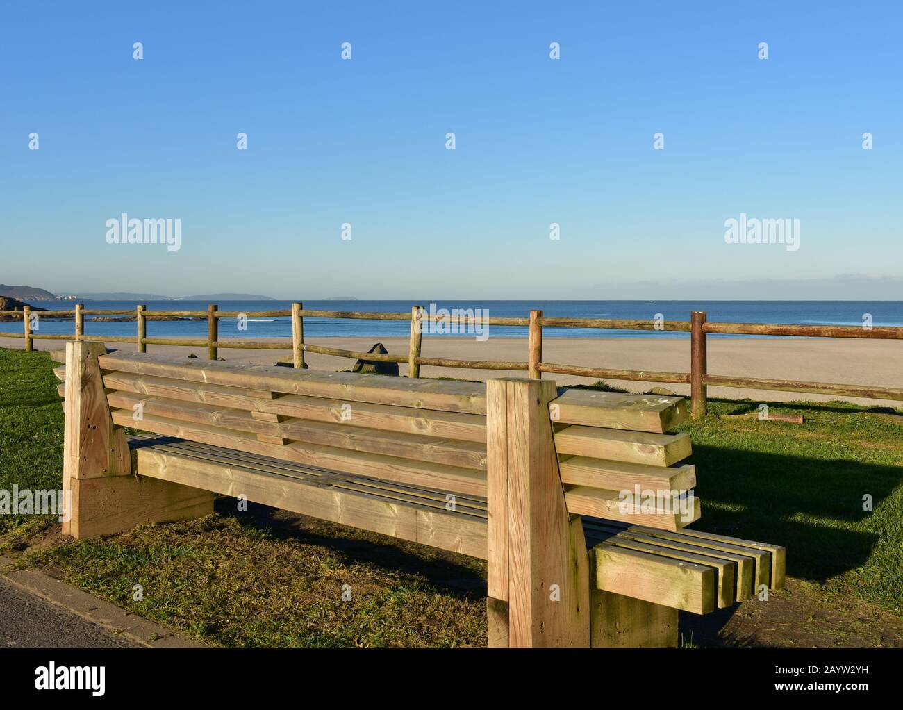 Wooden bench on a beach promenade with morning light and blue sky ...