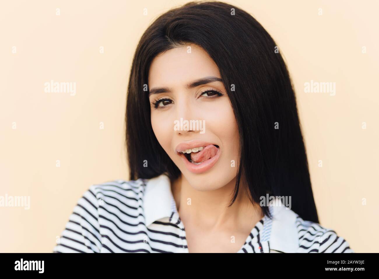 Portrait of attractive female model licks mouth with tongue, has ...