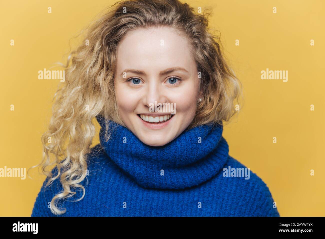 Happy delighted woman with light crisp hair, wears warm blue sweater ...