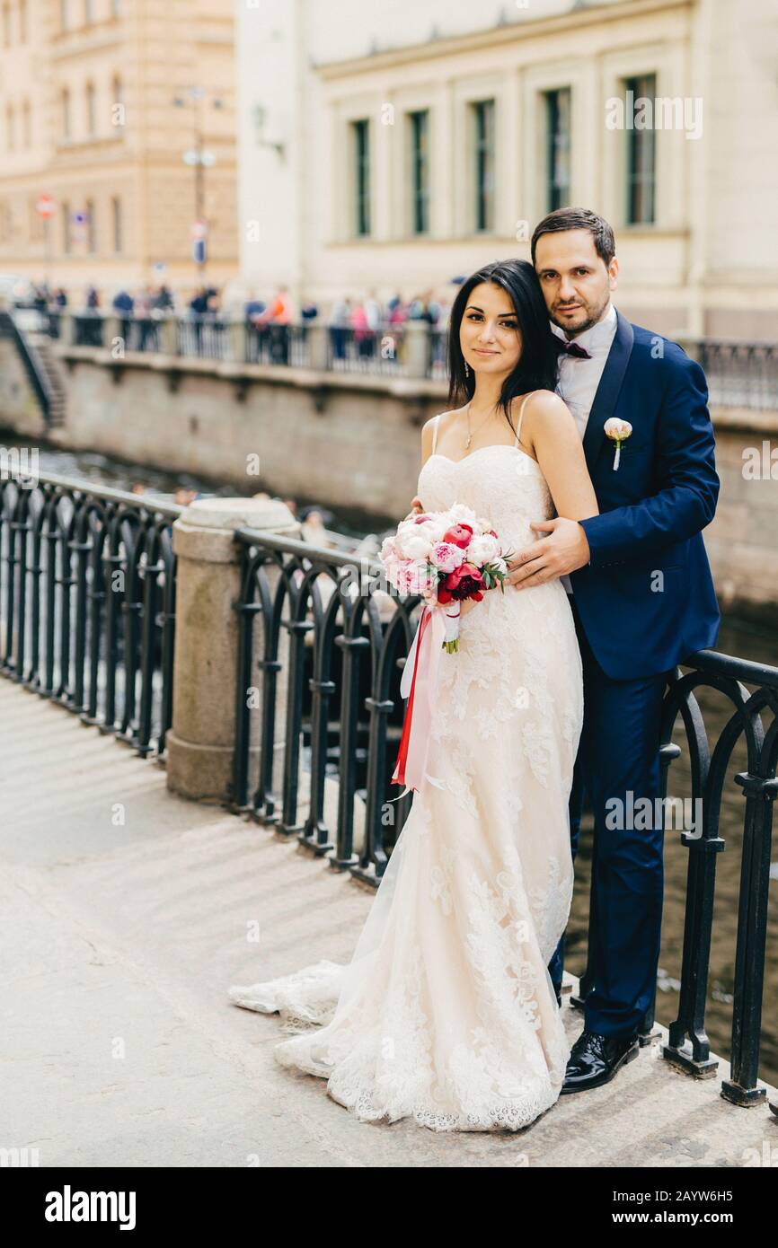 Handsome bearded bridegroom embraces his bride in white dress with ...