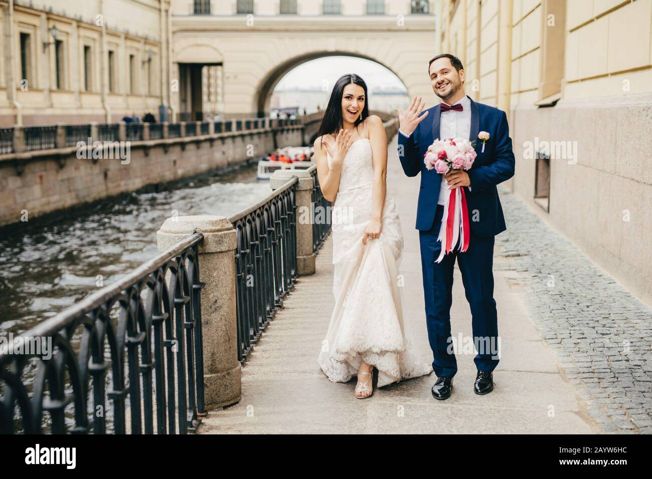 Excited married couple show rings on fingers, walk on bridge, poses at ...