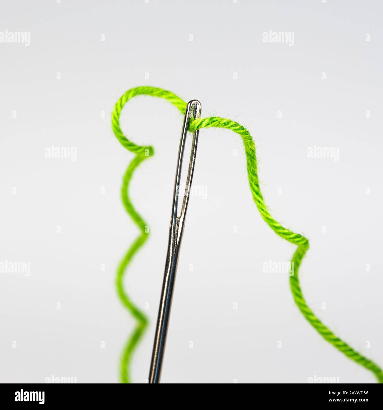 Green thread threaded into the eye of a needle. Close-up with shallow ...