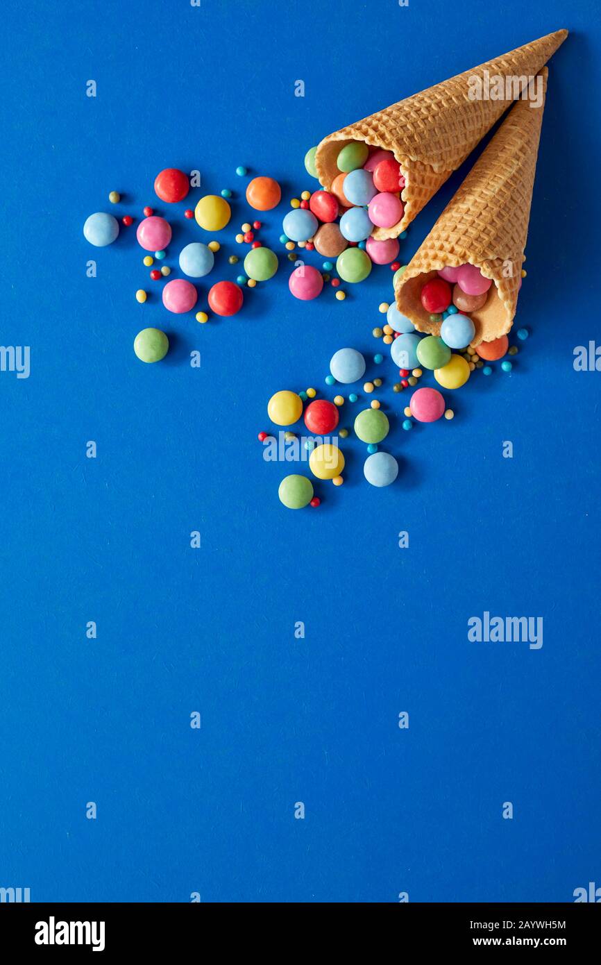 Rainbow colored sugar-coated candy spilling from two wafer cornets or ...