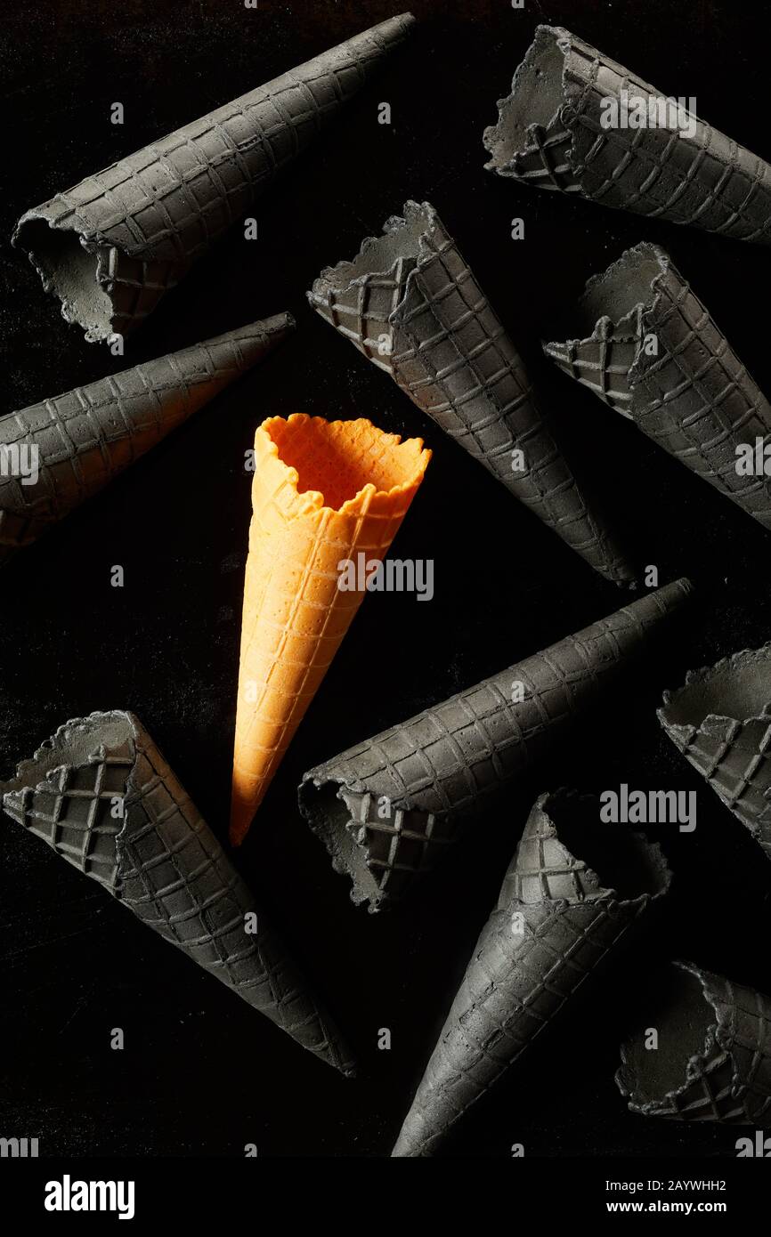 Single unique yellow ice cream cone amongst scattered grey cornets on a ...