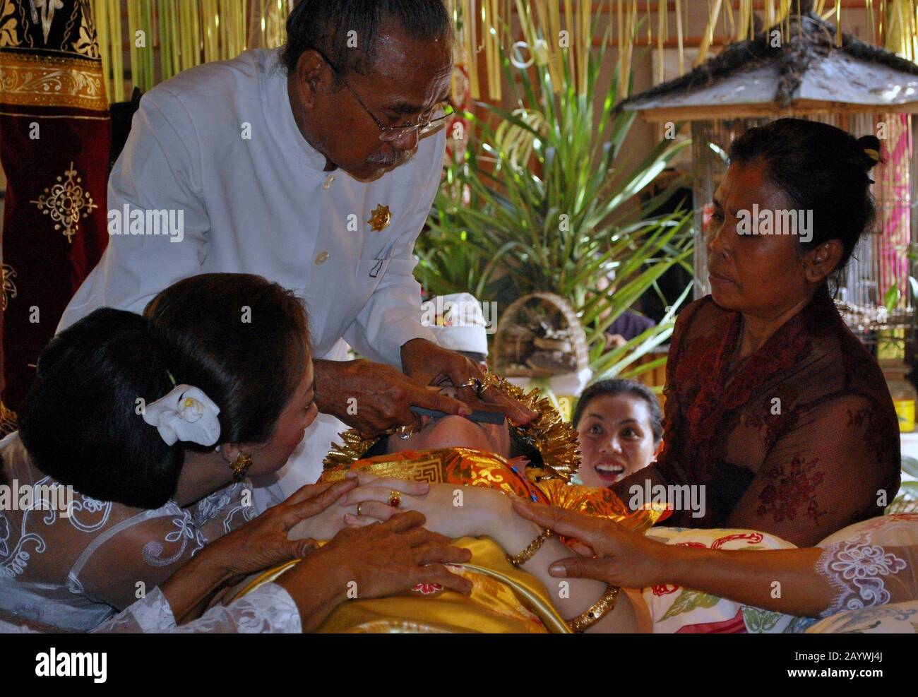 A Balinese woman is guided through a cutting teeth ritual. Cutting ...