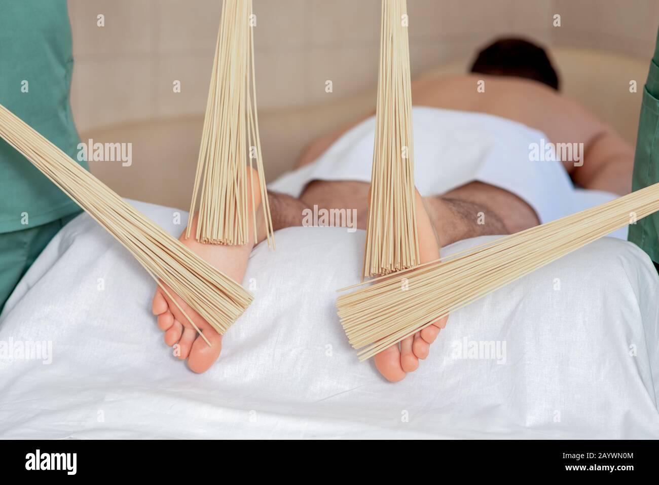Male receiving feet massage with bamboo brooms in four hands, close up ...