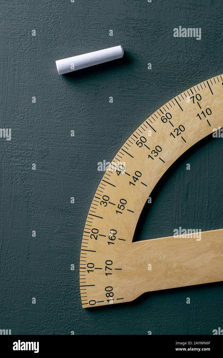 closeup of a protractor and a piece of chalk on a dark green chalkboard ...