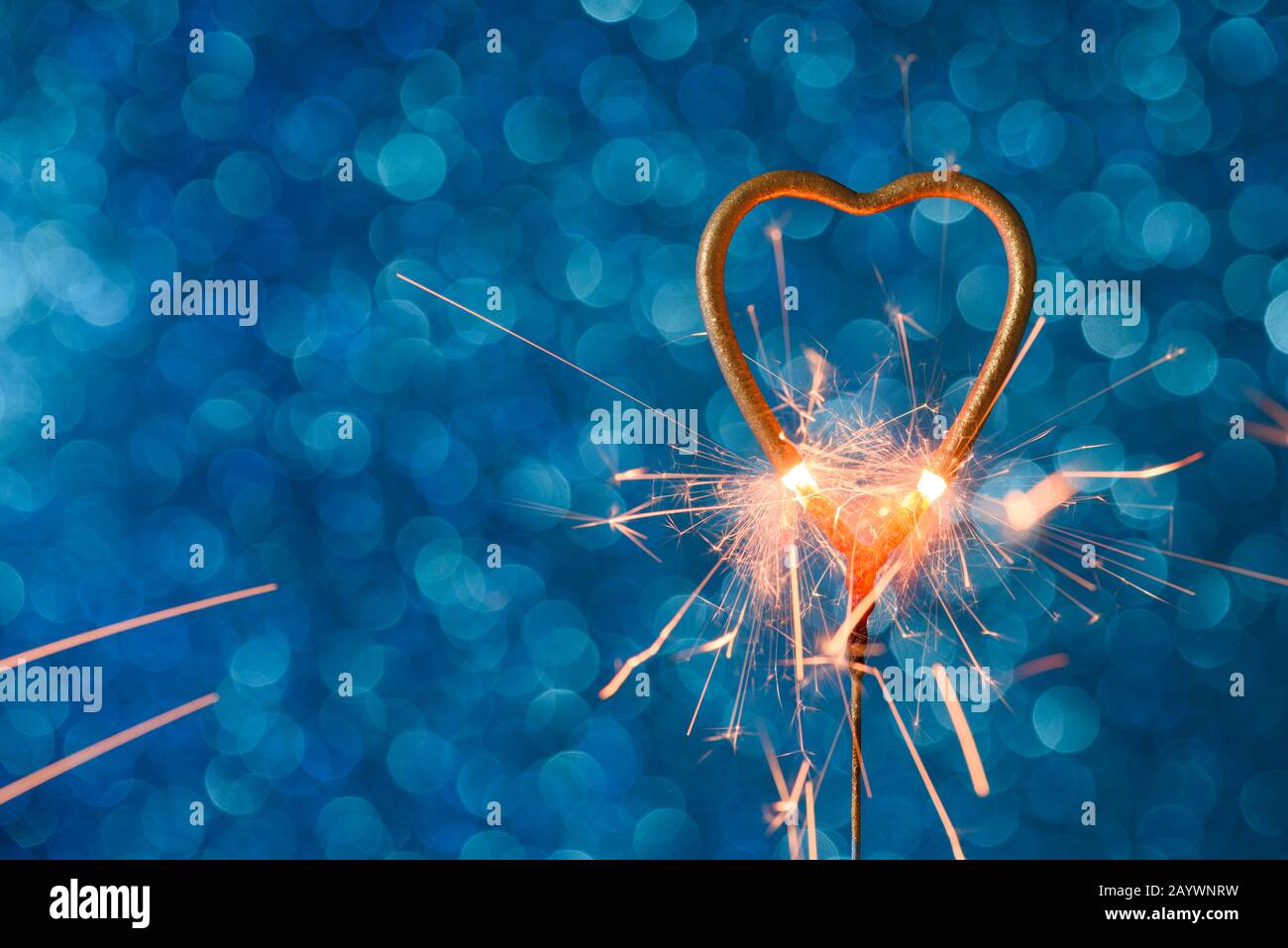 Sparkler in a shape of golden heat burning over blue bokeh background ...