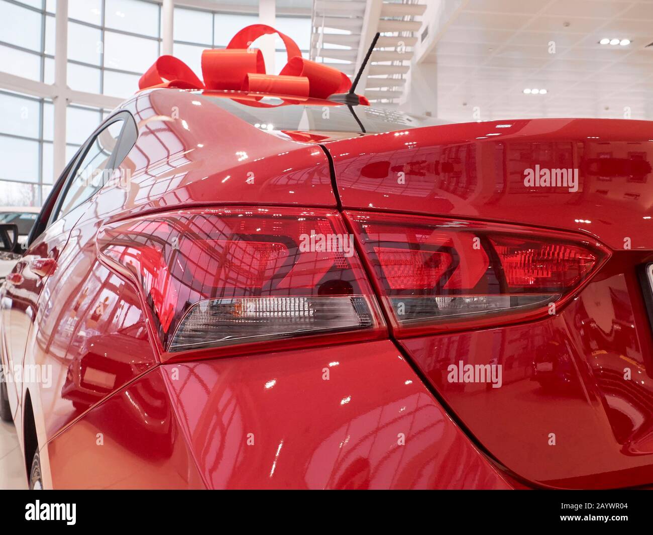 New red car with red gift ribbon atop in the car dealer showroom back ...