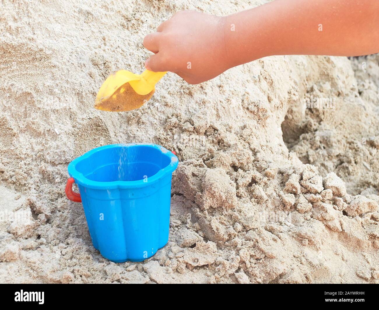 Hand of child playing in the sandbox with yellow scoop and blue bucket ...