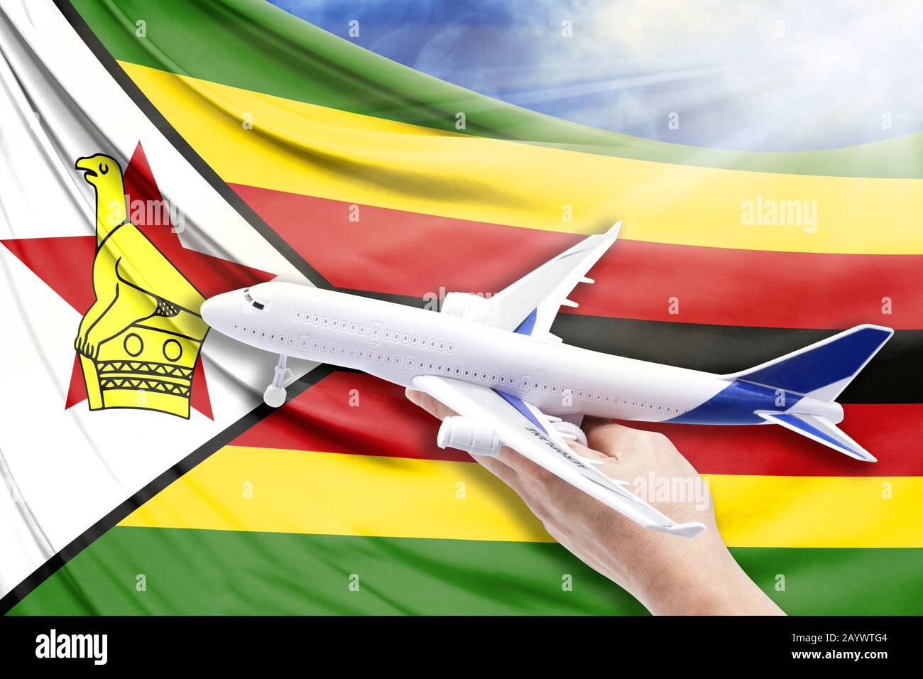 Airplane in hand with national flag of Zimbabwe on a background of blue ...