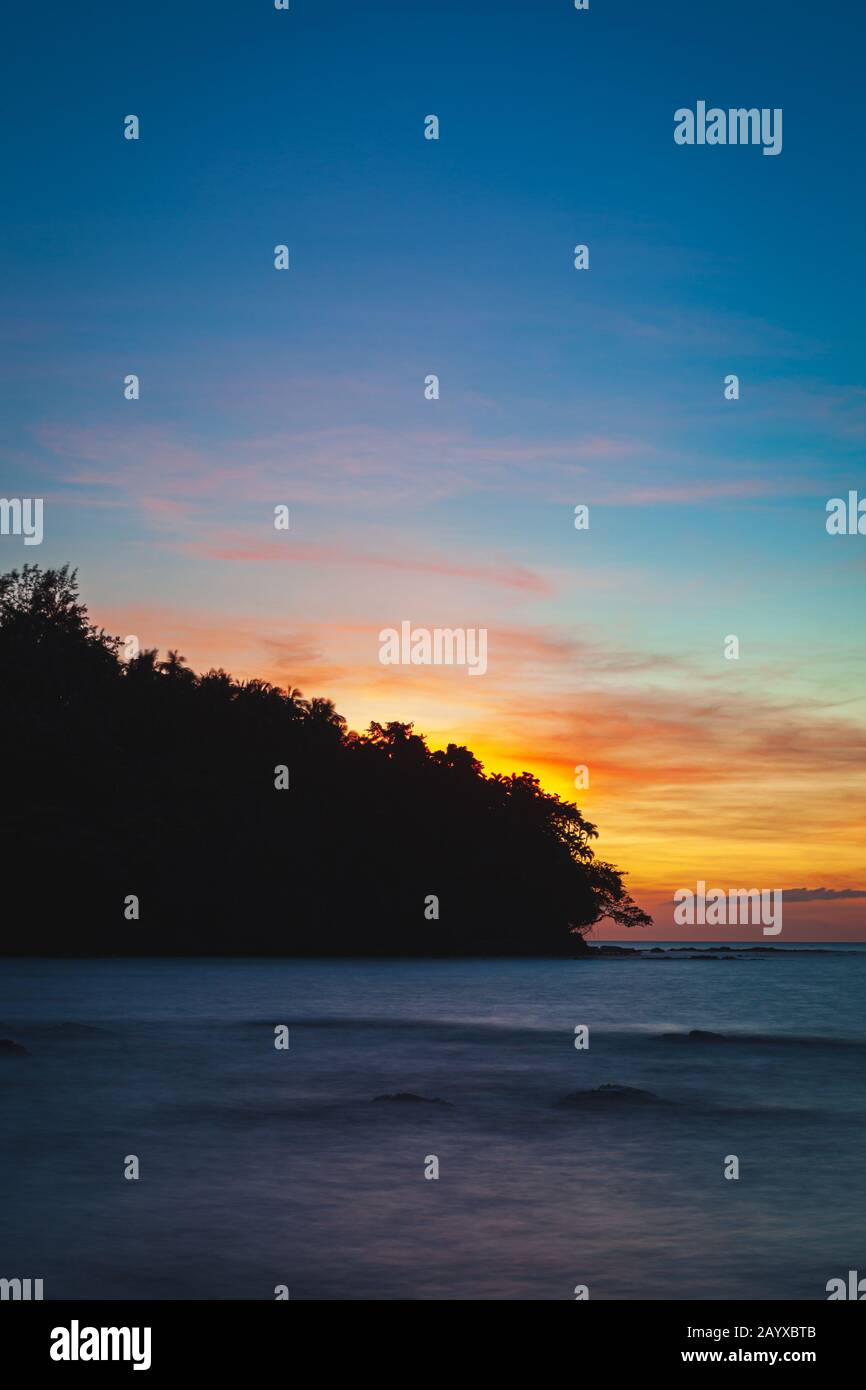 Vivid sunset sky waterscape and silhouette forest island background ...