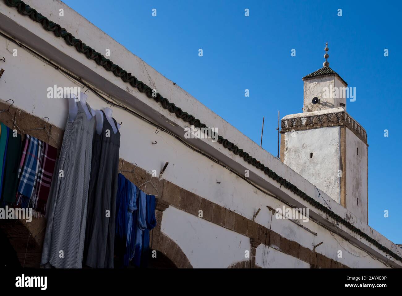 Tower of a mosque with weathered white facade and a line of the houses ...