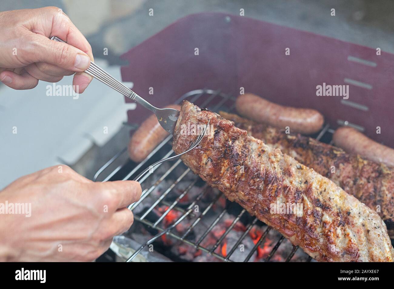 Hands turning pork chops roasted on the grill over the charcoal fire ...