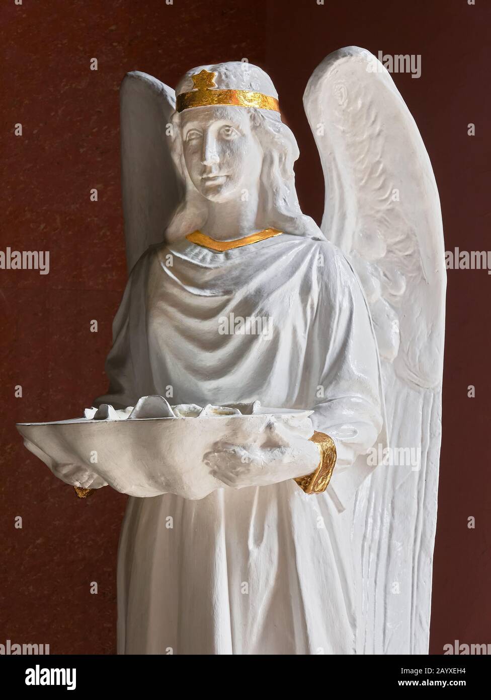 A white painted statue of an angel with golden star, holding a shell ...