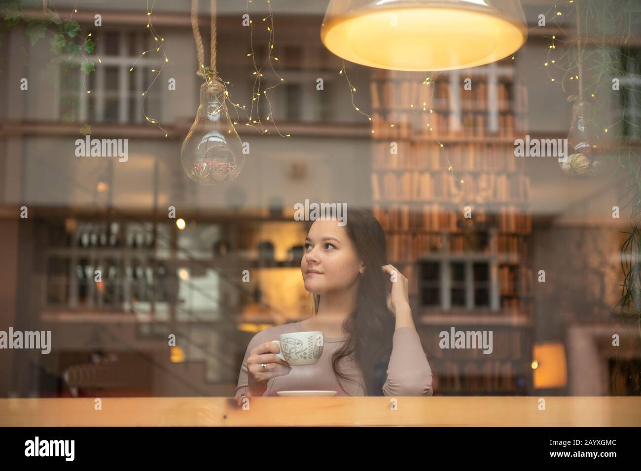 Woman sitting with cup of tea inside cafe, view through the window ...