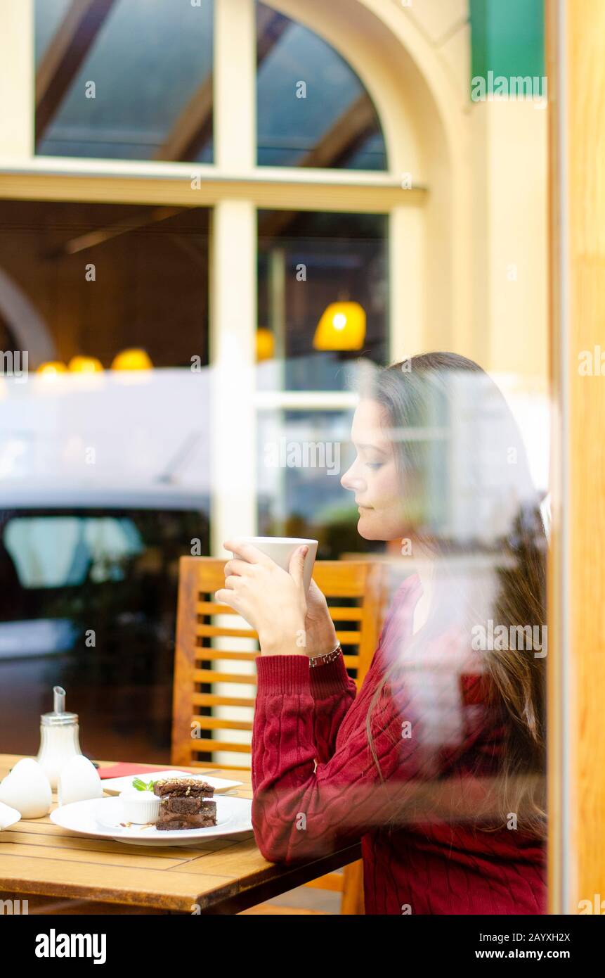 Woman sitting with cup of tea inside cafe, view through the window ...