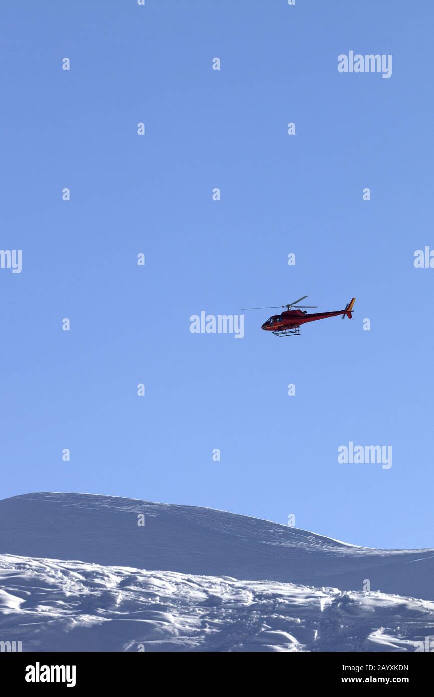 Helicopter in blue clear sky and snowy ski slope in high mountains at ...