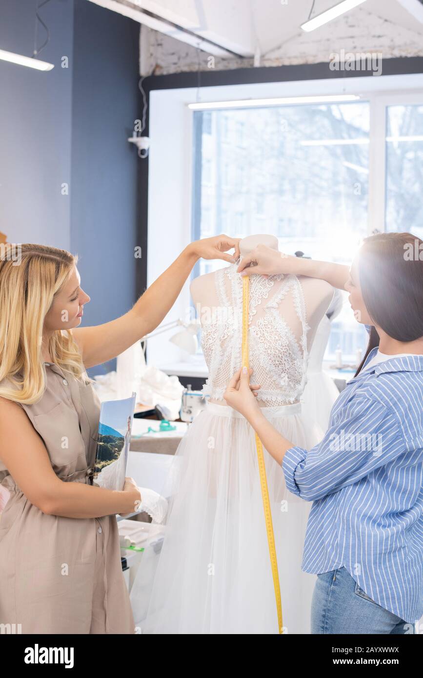 Two young bridal fashion designers working together on wedding gown in ...