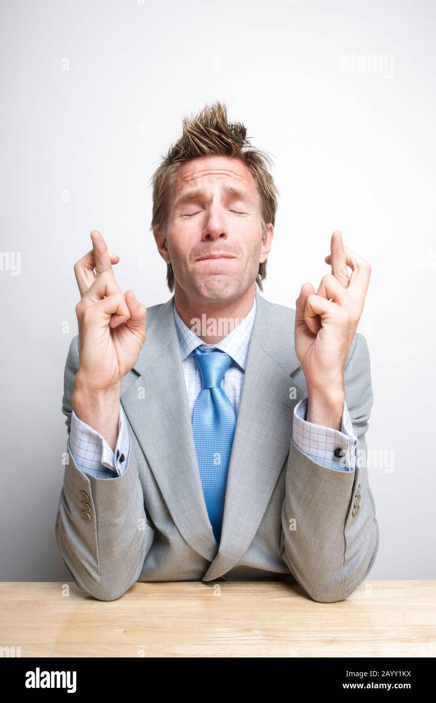 Nervous office worker sitting at his desk with his fingers crossed ...
