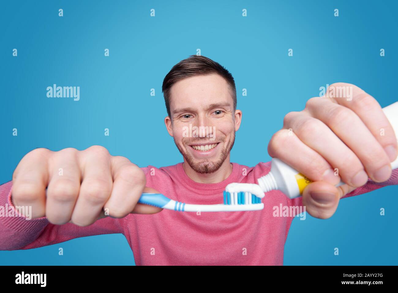 Smiling young man with beard holding toothbrush and applying toothpaste ...