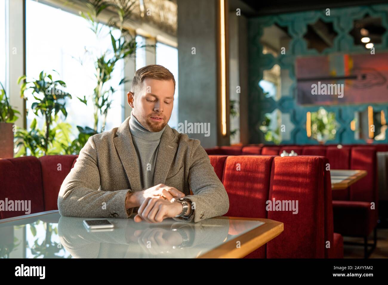 Caucasian man sitting alone in cafe looking at his wrist watch checking ...