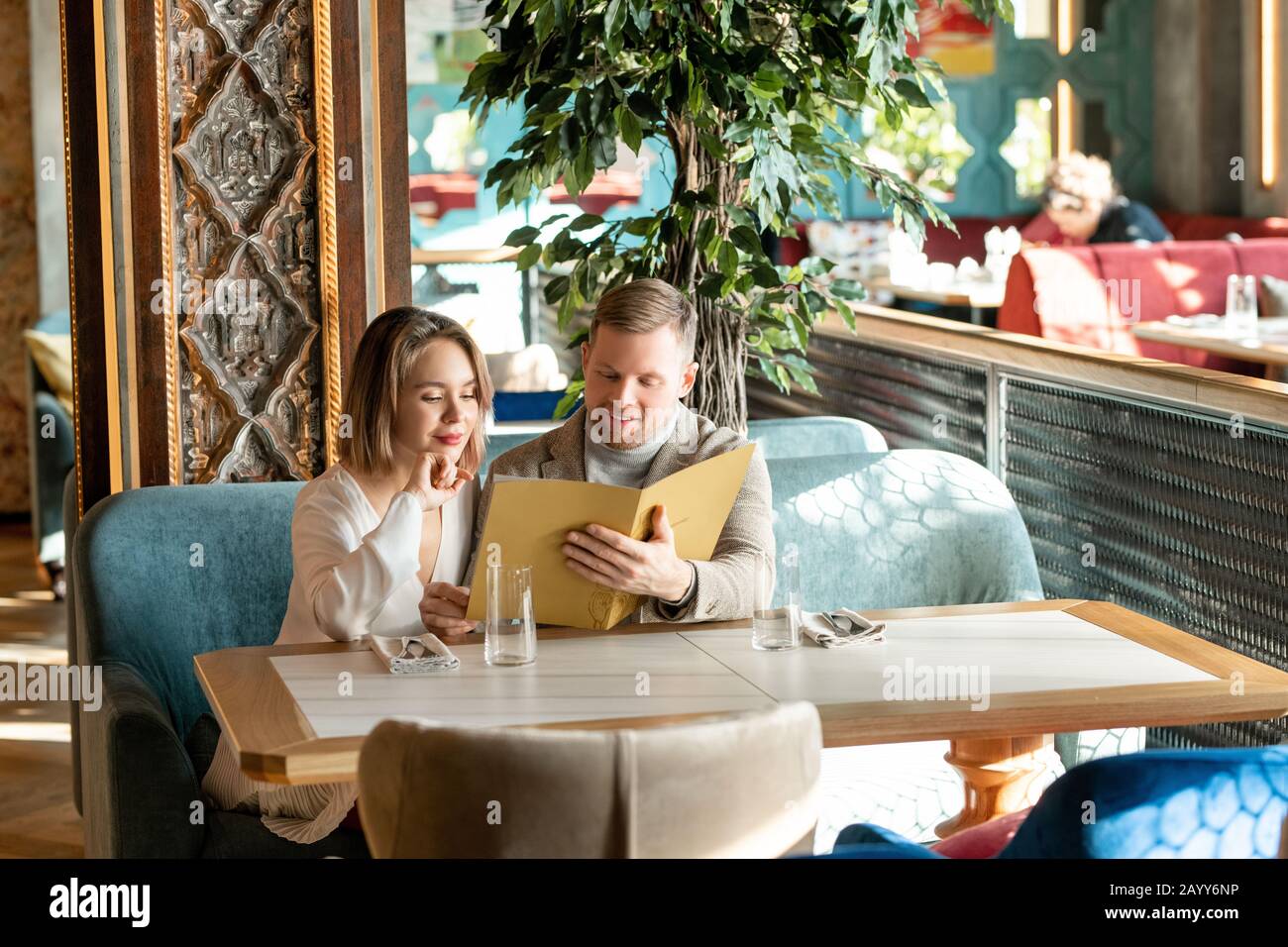 Horizontal shot of happy young adult man and woman looking through menu ...