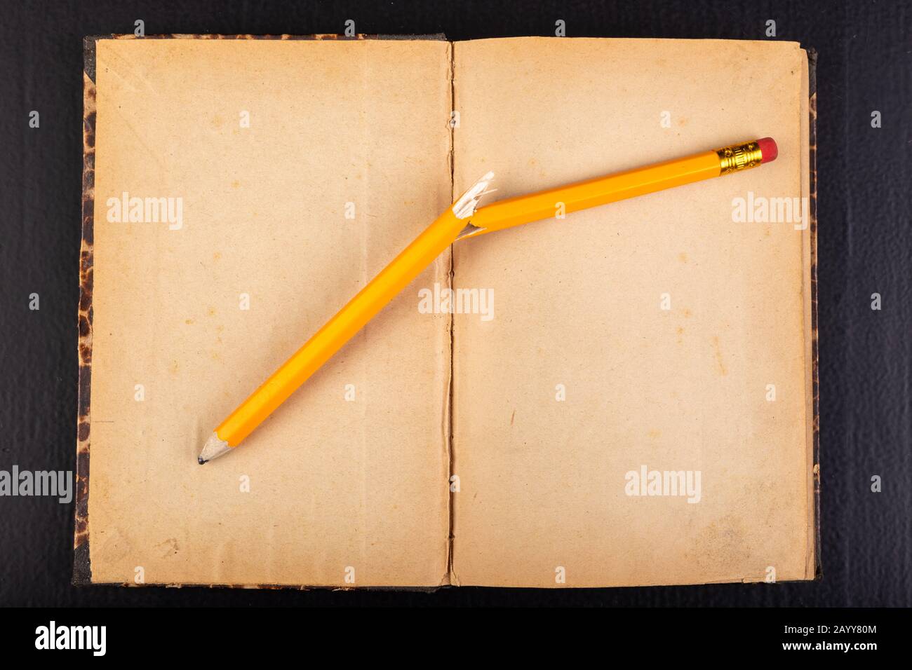 A broken pencil and an old book. Emotions during office work. Dark ...