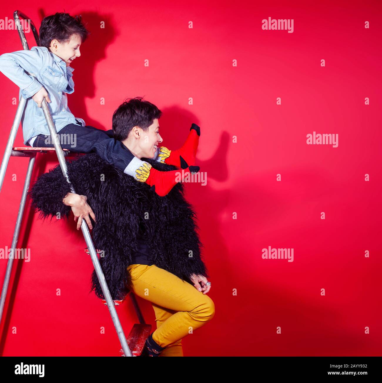 pretty young mother with little son on ladder on red background posing ...