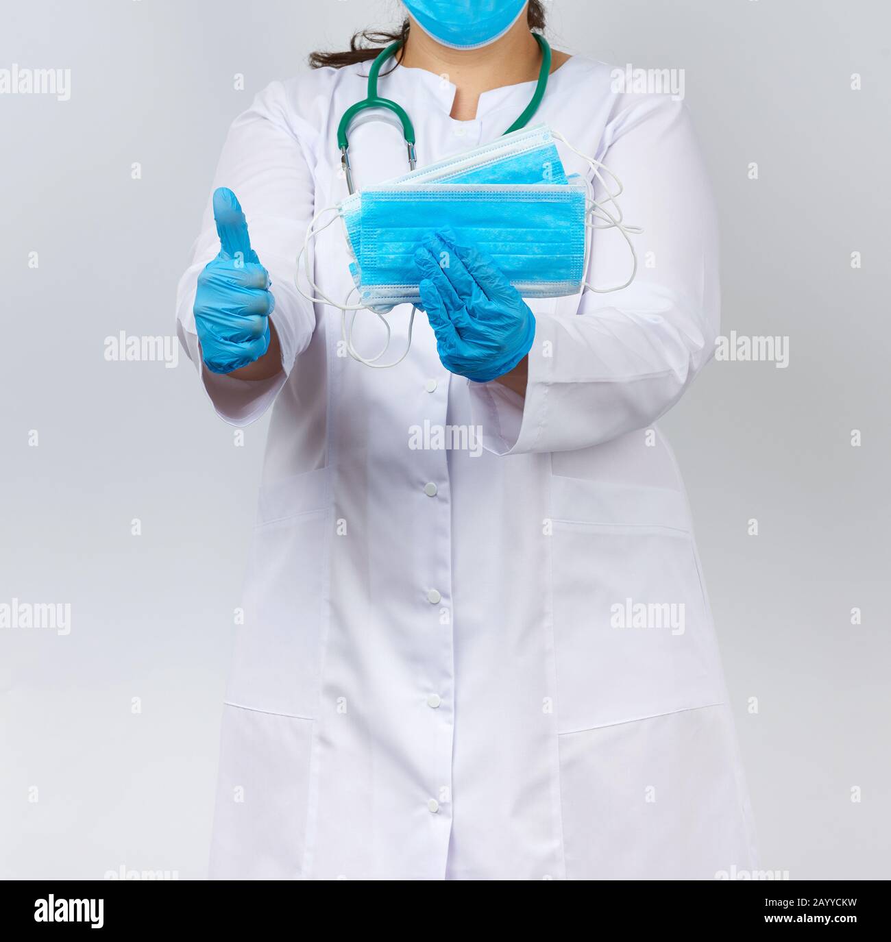 female doctor in a white coat and mask holds a stack of protective face ...