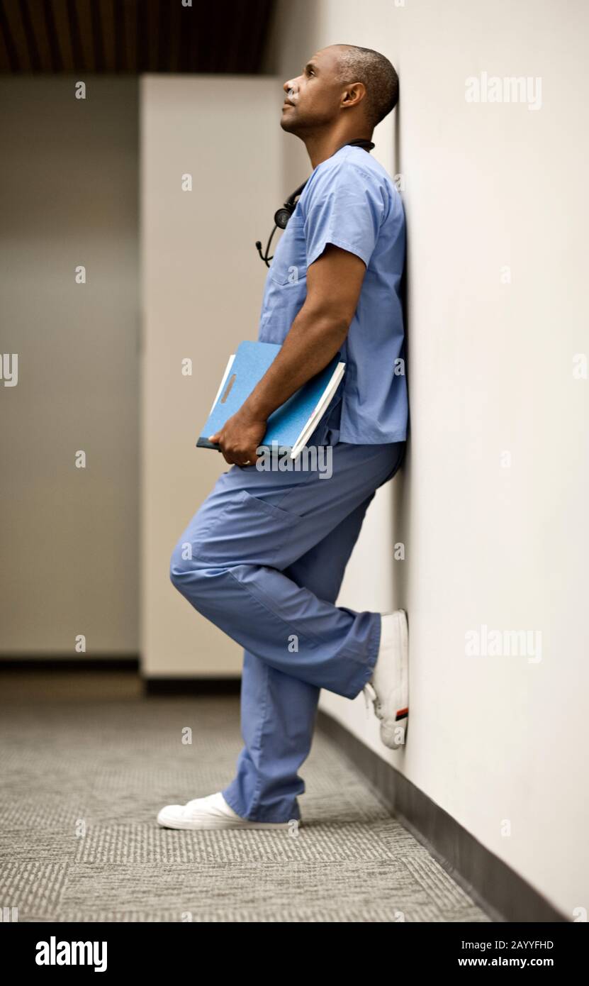 Male doctor leaning against a wall looking worried Stock Photo - Alamy