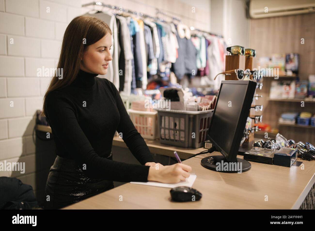 Young shop assistant in clothes store working by comtuper. Beautiful ...